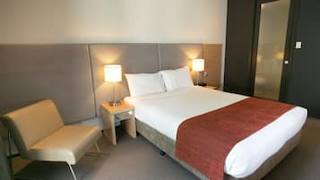 Quarto de hotel com cama, mesa de cabeceira, cadeira e duas luminárias.
