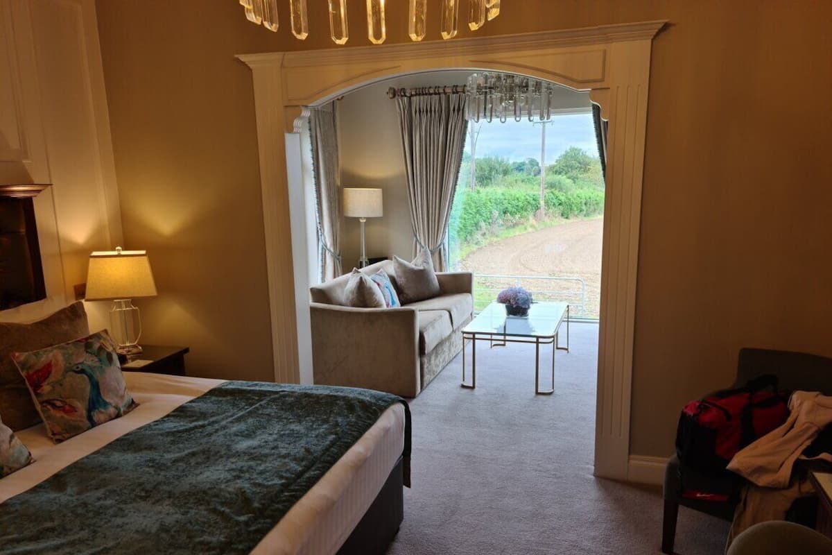 Um quarto com cama, mesa de cabeceira, luminária, sofá, mesa e vista para o exterior.