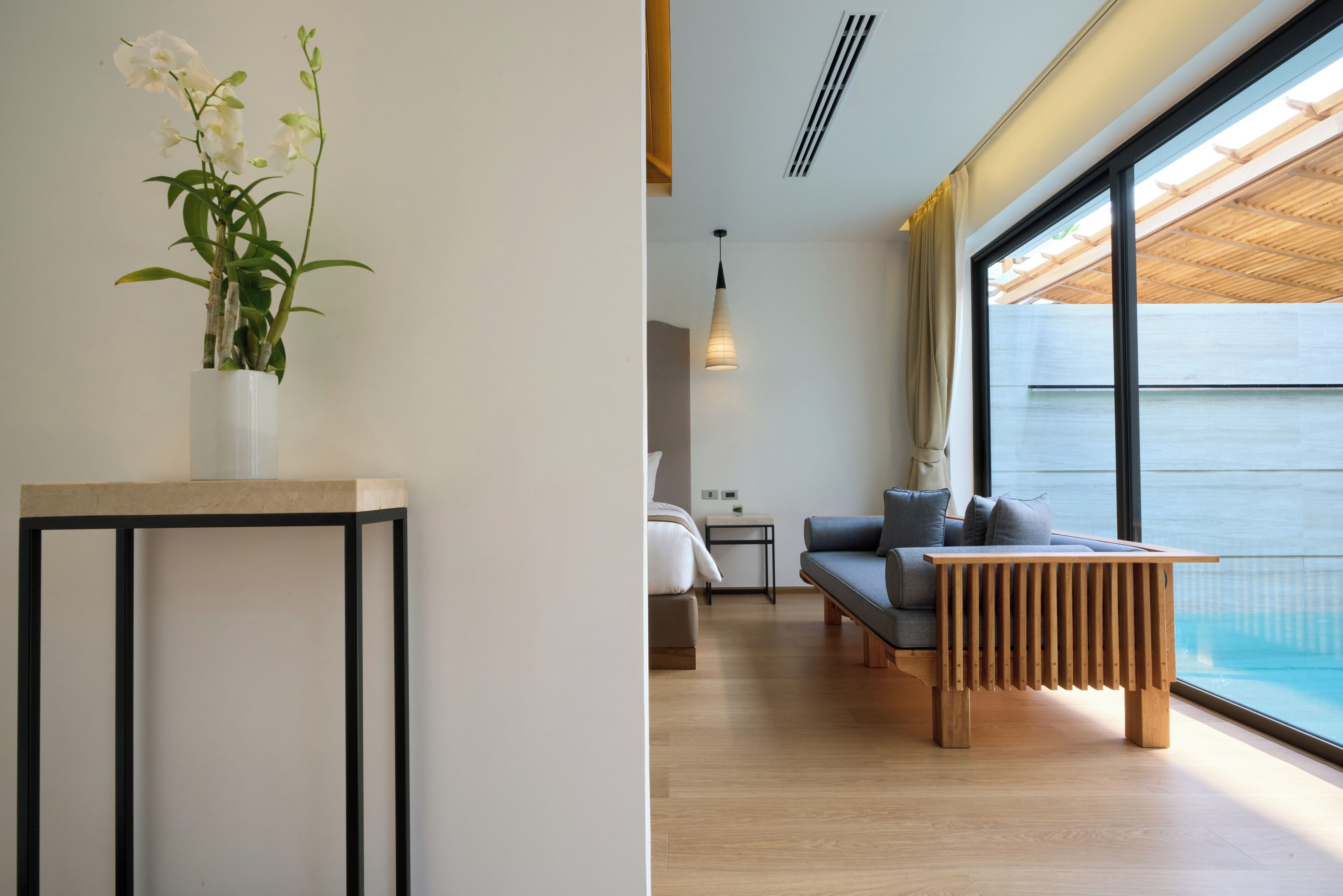 Quarto moderno com uma cama, um sofá, uma mesa de centro de madeira e um vaso com flores brancas sobre uma mesa de metal preto.