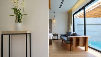 Quarto moderno com uma cama, um sofá, uma mesa de centro de madeira e um vaso com flores brancas sobre uma mesa de metal preto.