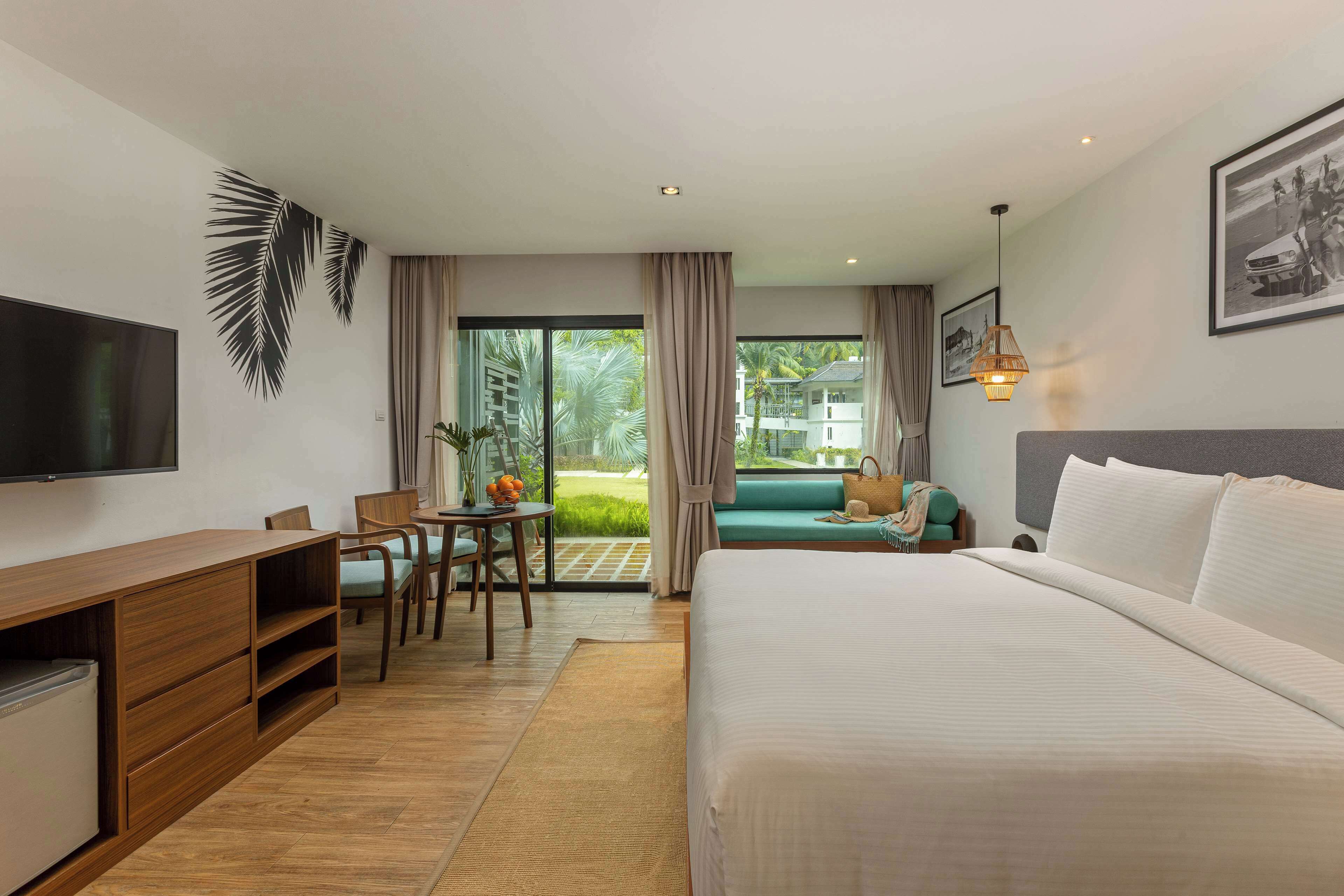 Quarto de hotel com cama, escrivaninha, televisão, sofá e vista para o exterior.