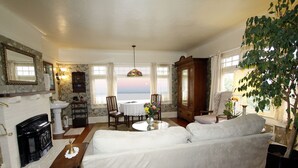Uma sala de estar com lareira, uma mesa de jantar com cadeiras, um sofá e uma janela grande com vista.