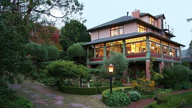 Uma casa grande de dois andares, com varanda coberta e jardim.