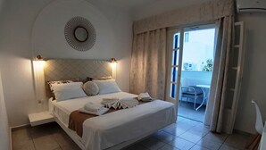 Uma cama bem arrumada com cabeceira, uma mesa de cabeceira com abajur, e vista para área externa por uma porta de correr.