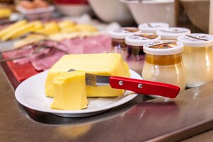 Um prato com um bloco de manteiga e uma faca, rodeado por potes de acompanhamentos.