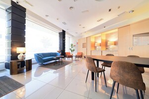 Um hall de hotel moderno com sofá, cadeiras, uma mesa de jantar e cozinha.