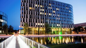 Um hotel moderno com piscina refletora, uma passarela e fachada bem iluminada.