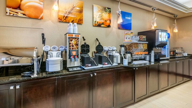 Uma área de recepção de hotel com um espaço para café, incluindo várias máquinas de café, um aparelho para waffles e uma variedade de condimentos e utensílios.