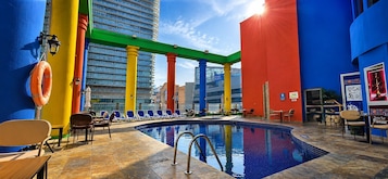Uma área de piscina no terraço com vista clara para o horizonte da cidade, incluindo um edifício com fachada de vidro em destaque.