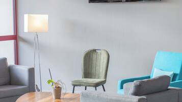 Uma sala de estar moderna com uma TV de tela plana na parede, uma mesa de centro redonda de madeira e duas poltronas.