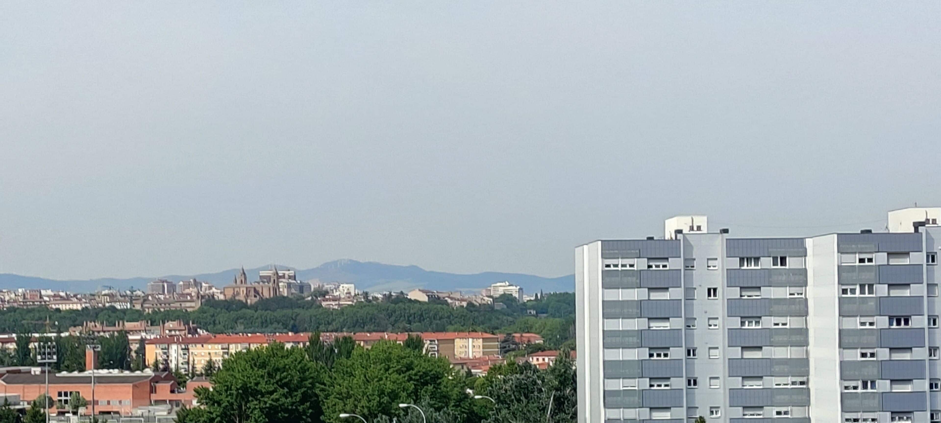 Paisagem urbana com edifícios modernos, uma igreja em destaque e montanhas ao longe.