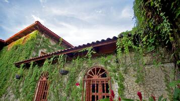 Um edifício com paredes de pedra e varandas de madeira, coberto por trepadeiras verdes.