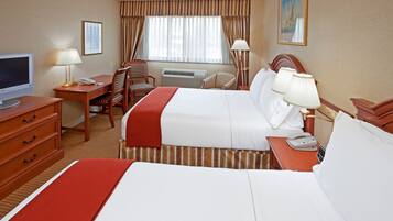 Quarto de hotel com cama, escrivaninha com computador, cadeira, televisão e janela com cortinas.