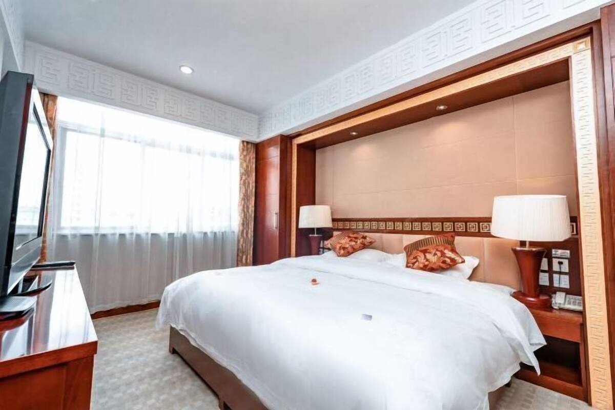 Quarto de hotel com uma cama grande, televisão, escrivaninha com cadeira e janela com cortinas.
