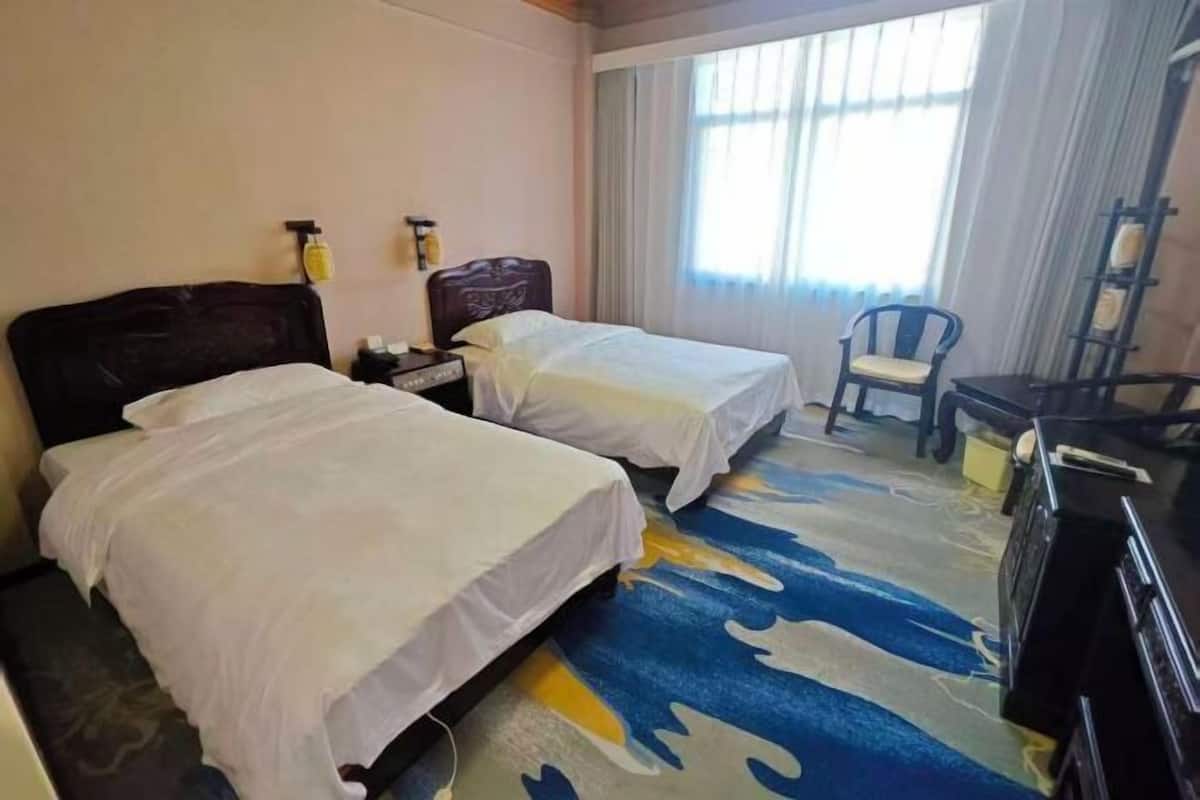 Quarto de hotel com duas camas, uma escrivaninha, uma cadeira e uma janela com cortinas.