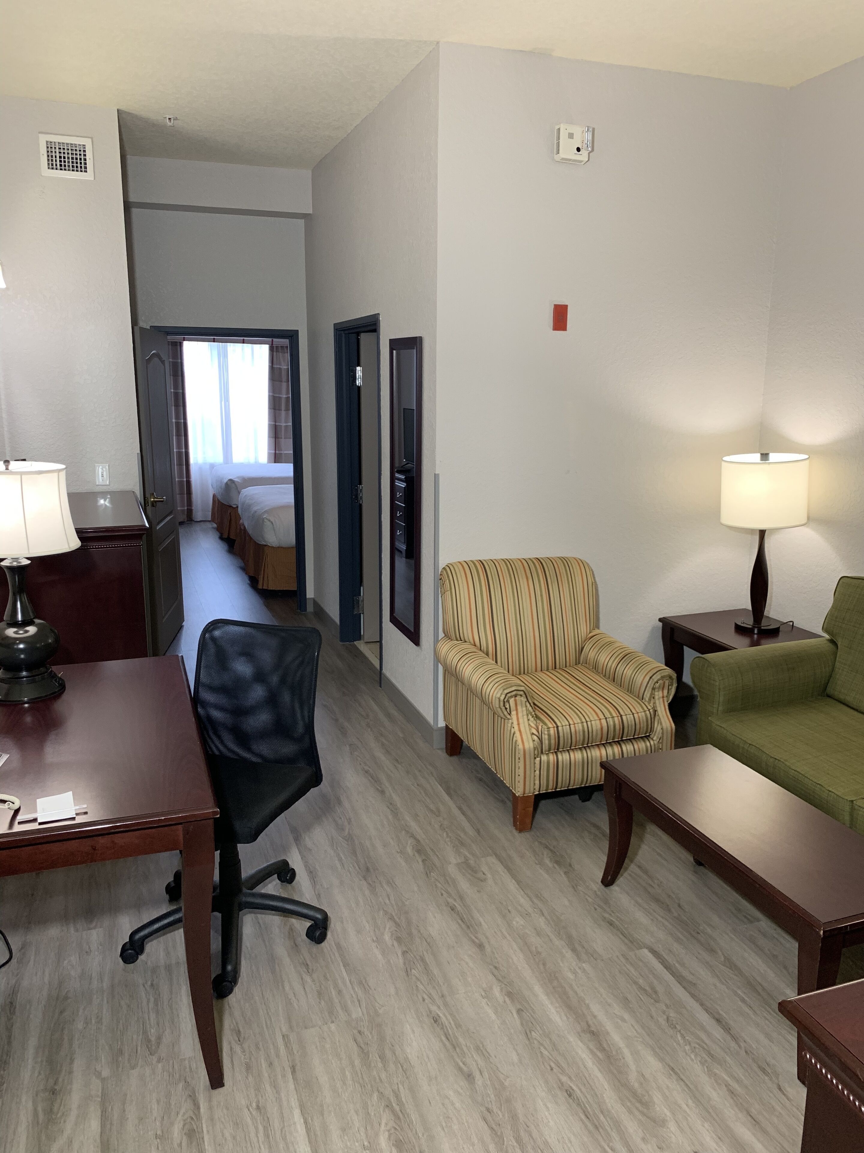 Quarto de hotel com secretária, cadeira de escritório, poltrona listrada, sofá e cama com vista para a janela.
