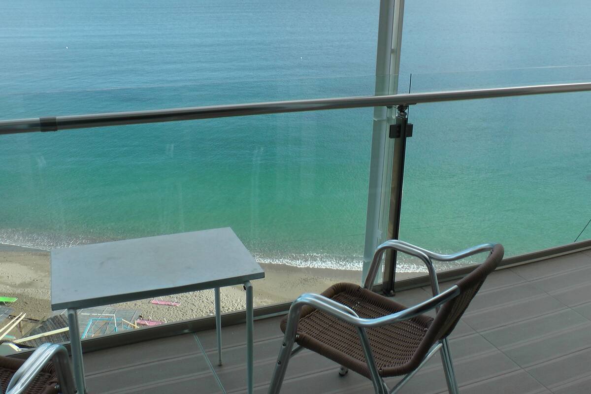 Varanda com mesa e cadeira, com vista para a praia e o oceano.