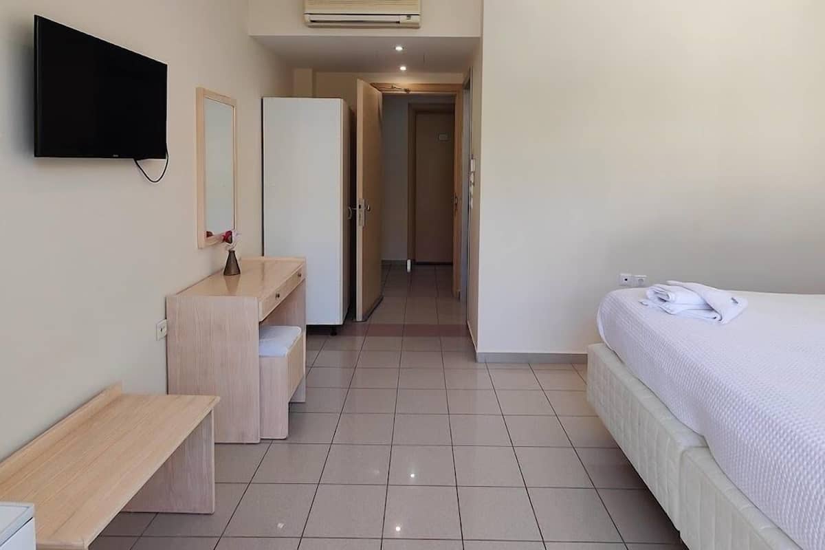 Quarto de hotel com uma cama, uma mesa, uma cadeira, uma televisão e um aparelho de ar condicionado.