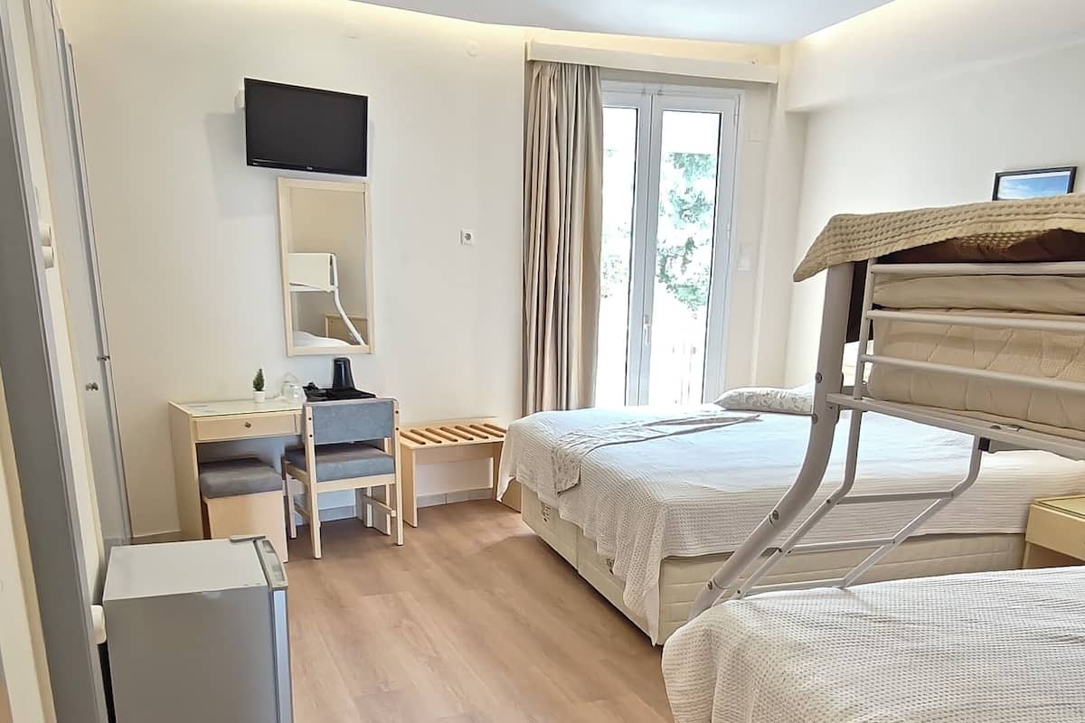 Quarto de hotel com duas camas, uma escrivaninha, uma cadeira, uma televisão e um ventilador de teto.