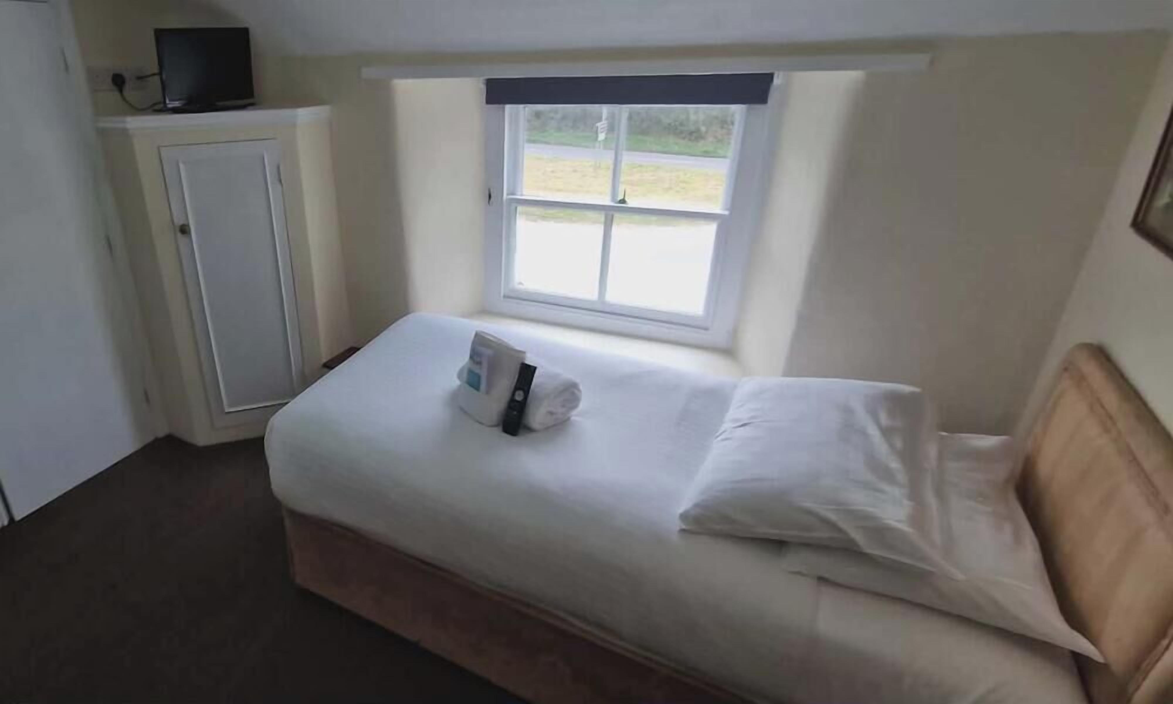 Quarto pequeno com uma cama de solteiro, janela, guarda-roupa e televisão em uma prateleira.