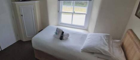 Quarto pequeno com uma cama de solteiro, janela, guarda-roupa e televisão em uma prateleira.