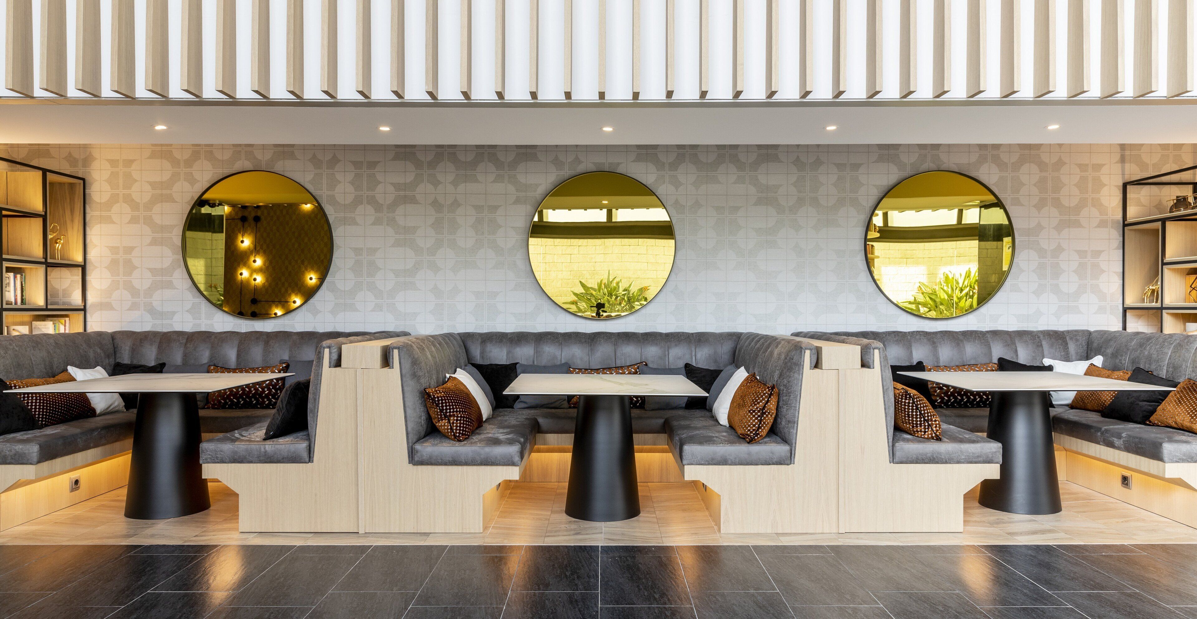 Uma área de estar moderna com sofás, uma mesa central e três espelhos grandes na parede.
