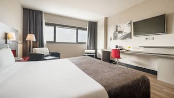 Quarto de hotel com uma cama grande, uma escrivaninha com cadeira, televisão e janela com cortinas.