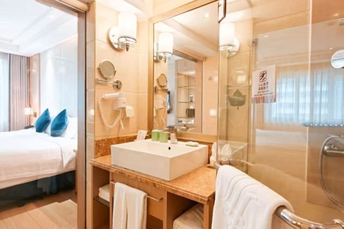 Quarto de hotel com cama, banheiro com pia, espelho e chuveiro.