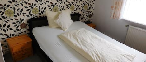 Quarto com cama, duas mesas de cabeceira, uma gaveta de madeira e papel de parede com padrão floral.