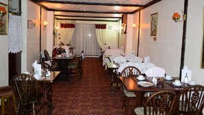 Uma sala de jantar com uma mesa comprida, cadeiras e piso coberto por carpete. Há cortinas e arandelas nas paredes.