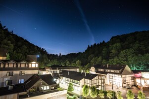 Uma aldeia europeia tradicional à noite, com edifícios iluminados e um céu estrelado.