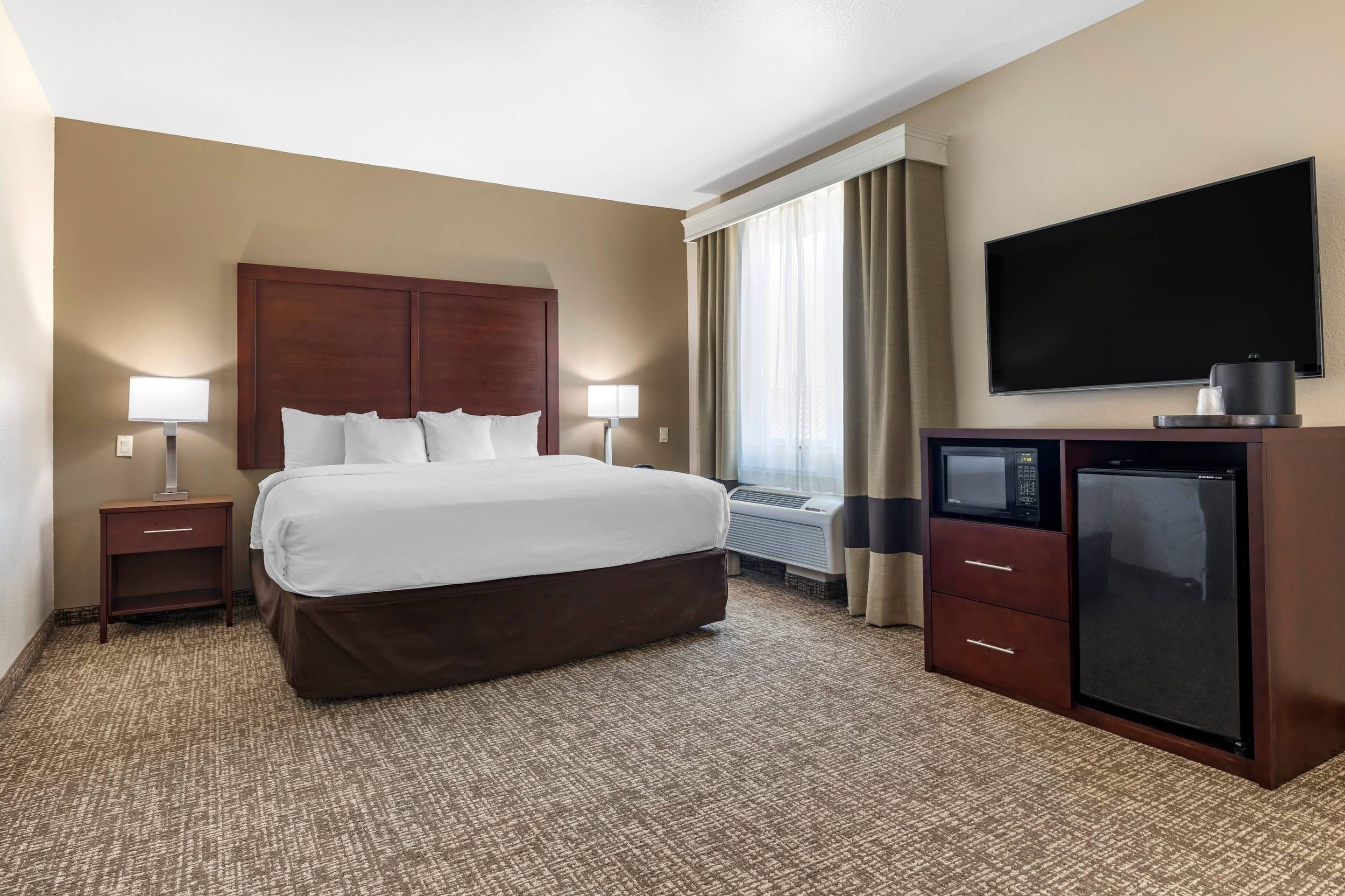 Quarto de hotel com uma cama grande, televisão de tela plana, minibar e ar condicionado.
