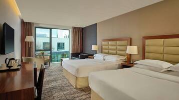 Quarto de hotel com duas camas, uma escrivaninha, uma cadeira, televisão e varanda com vista.
