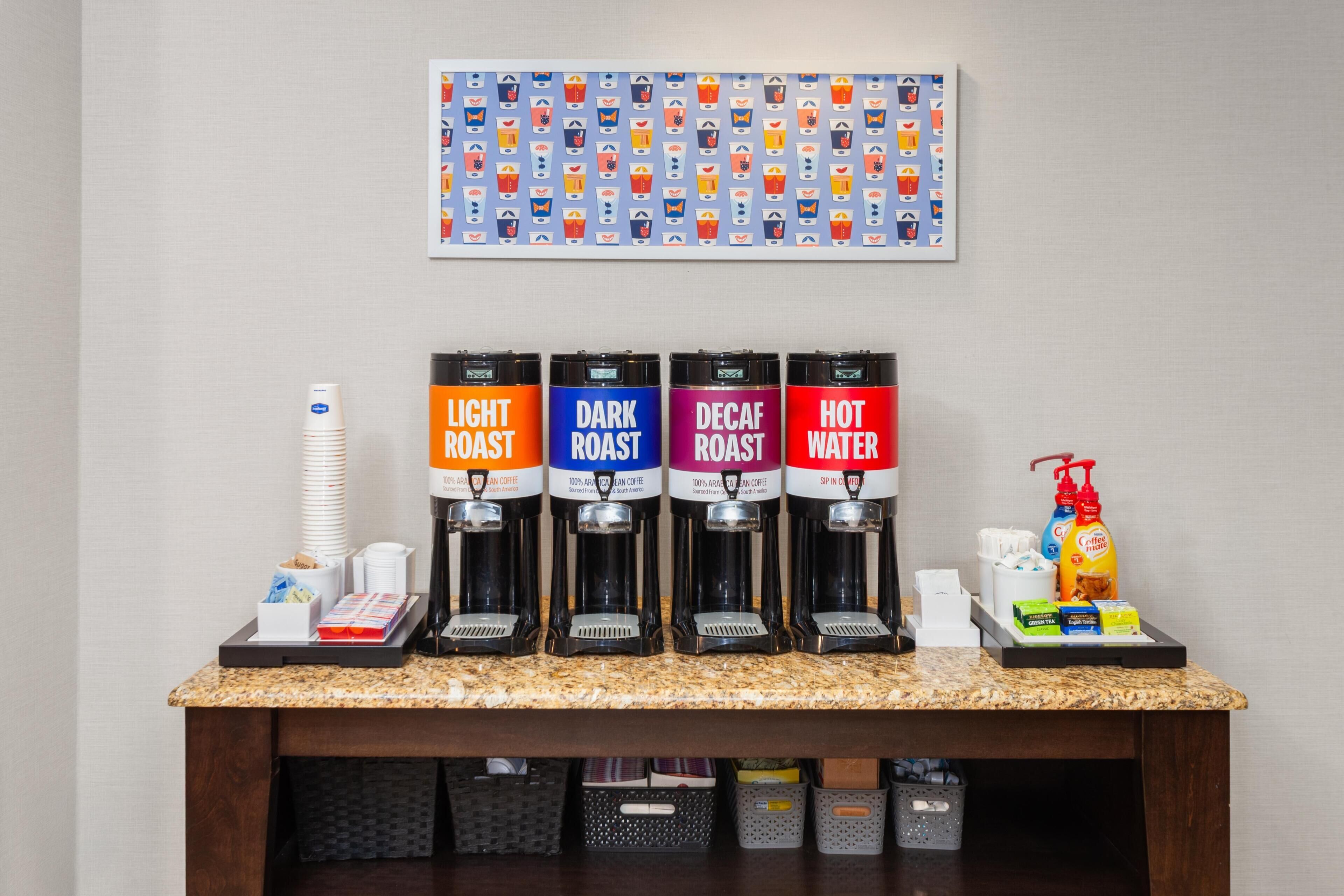 Uma estação de café com quatro dosadores identificados como Café Claro, Café Escuro, Café Descafeinado e Água Quente.