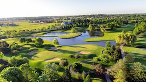 Um campo de golfe com obstáculos aquáticos, um clube e vegetação ao redor.
