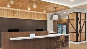 Bancada de recepção com teto de madeira, luminária pendente e frigobar abastecido com bebidas.