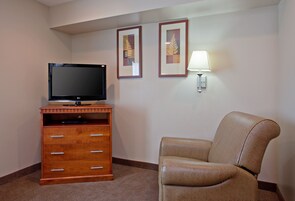 Quarto de hotel com televisão de tela plana em suporte de madeira, uma cadeira e duas imagens emolduradas na parede.