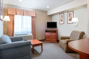 Quarto de hotel com sofá, mesa de madeira, televisão, armário e cadeira.