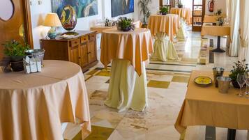 Um espaço de refeições de hotel com várias mesas, obras de arte nas paredes e chão xadrez.