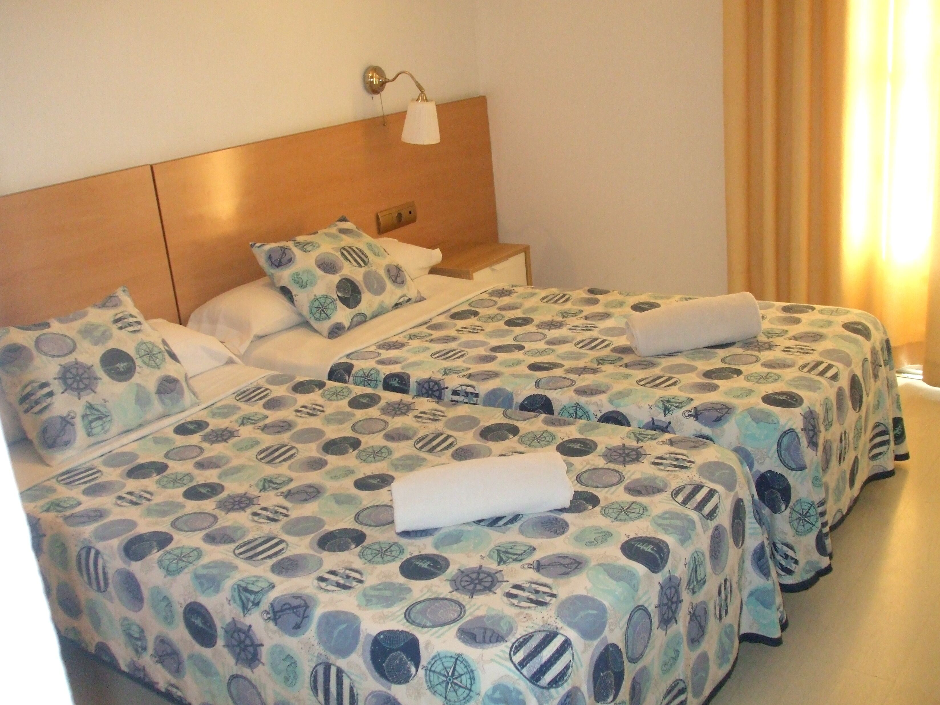 Uma cama de casal com cabeceira, duas almofadas, mesa de cabeceira e abajur.