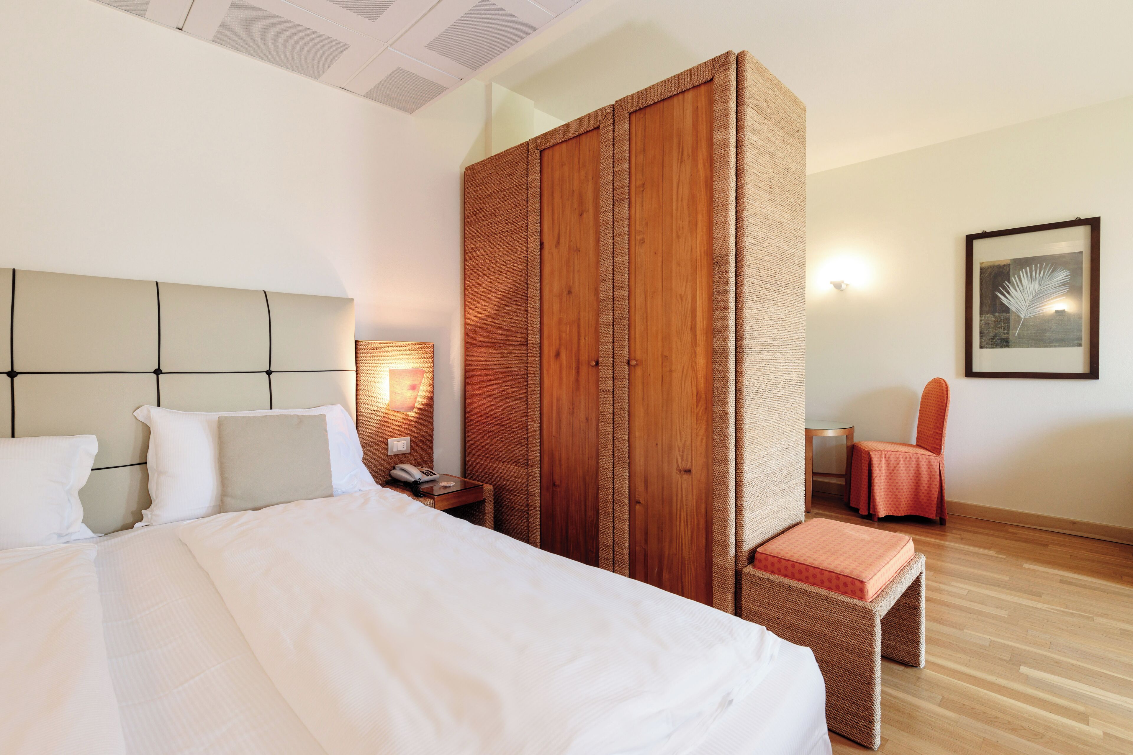 Quarto de hotel com cama grande, armário de madeira, mesa pequena, cadeira e luminária na parede.