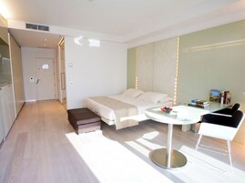 A modern hotel room with a bed, bedside table, and a small seating area.
