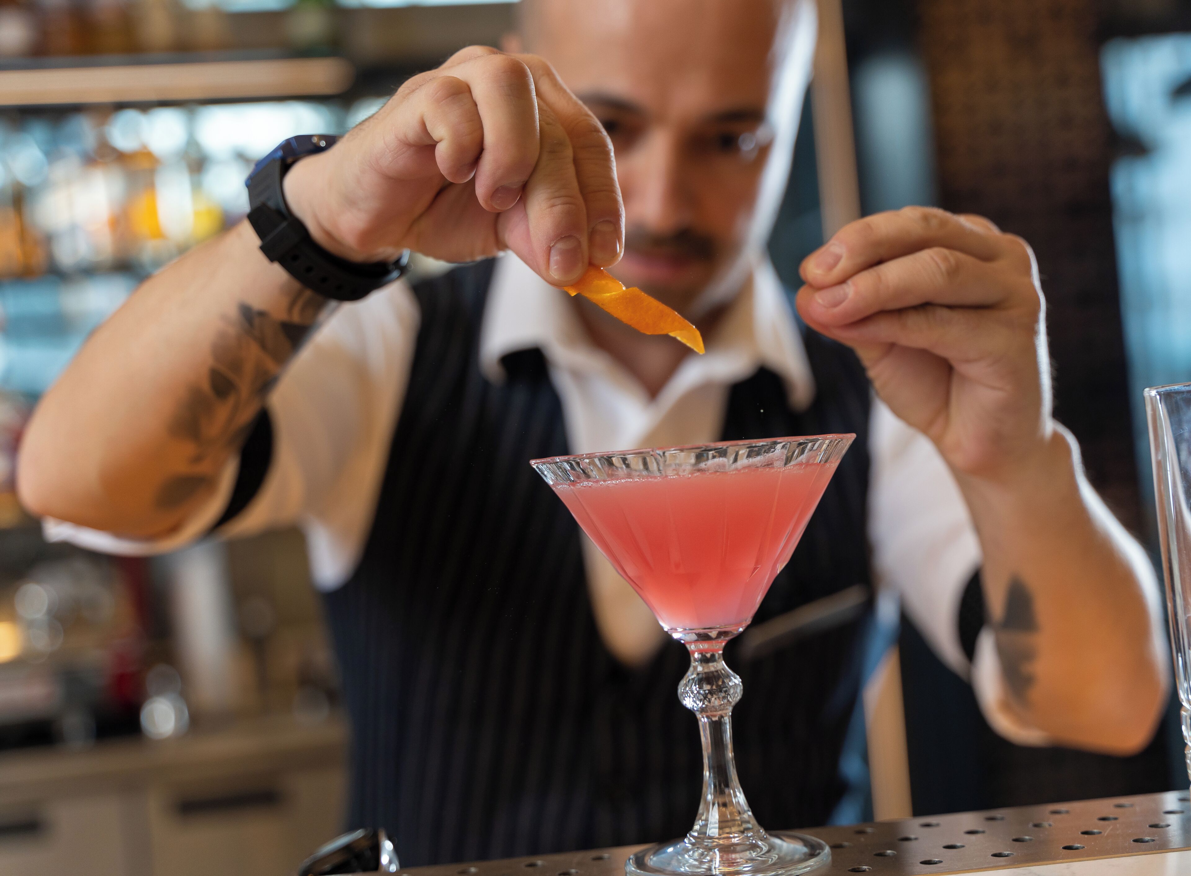 Um bartender prepara um cocktail rosa num copo de martini.