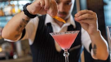 Um bartender prepara um cocktail rosa num copo de martini.