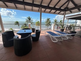 Uma área de estar coberta ao ar livre com vista para o oceano, com móveis de vime e uma mesa.