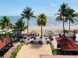 Um restaurante à beira-mar com mesas ao ar livre, palmeiras e vista para o oceano.
