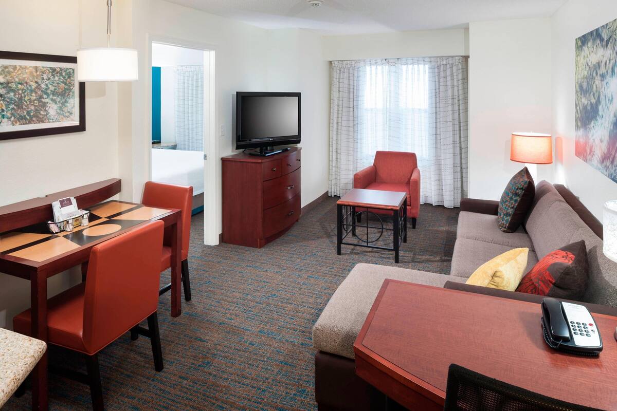 Quarto de hotel com área de refeições, sofá, televisão e telefone.