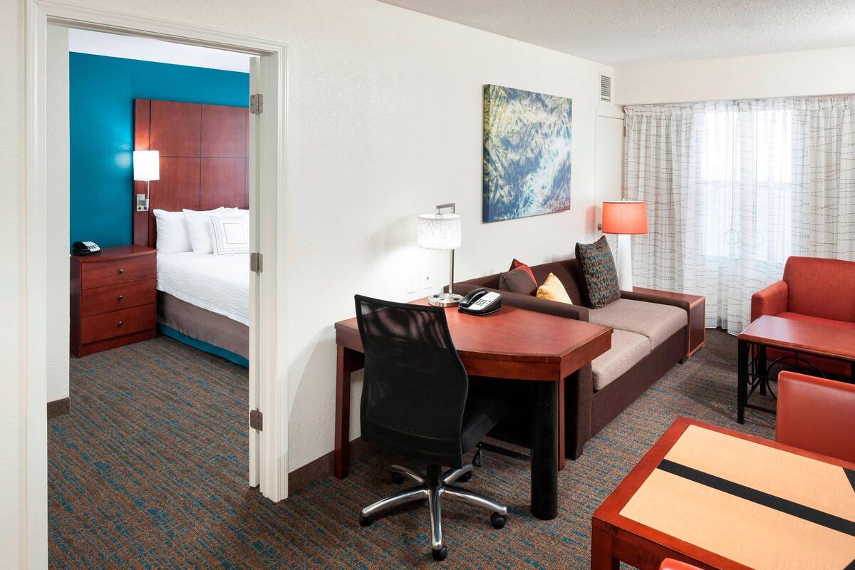 Quarto de hotel com cama, escrivaninha, cadeira, sofá e uma pequena mesa.