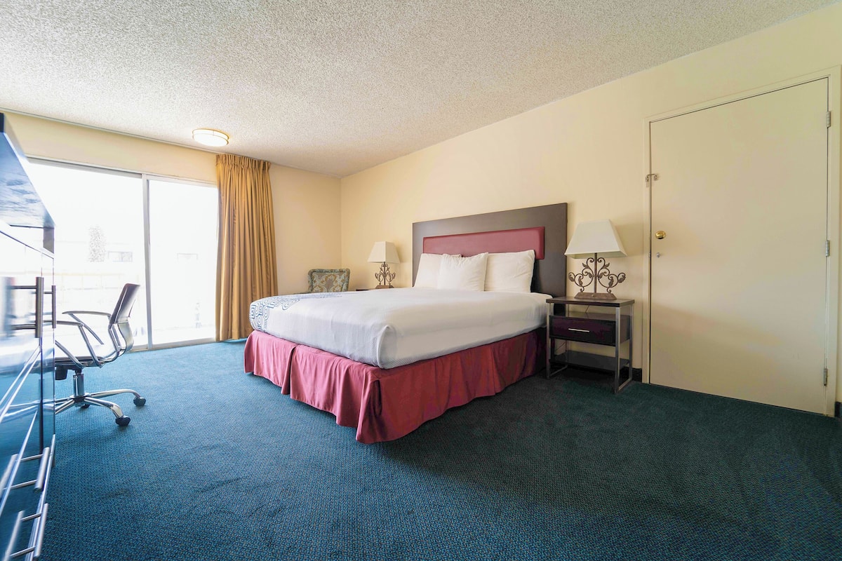 Quarto de hotel com uma cama grande, uma escrivaninha, uma cadeira e uma janela com cortinas.
