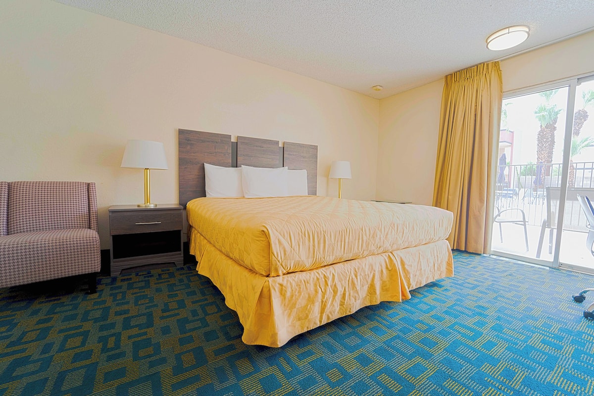 Quarto de hotel com uma cama grande, duas mesas de cabeceira com abajures, uma cadeira e vista para o exterior através de uma grande janela.